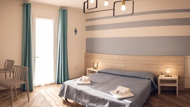 Um quarto com uma cama, duas mesas de cabeceira, uma cadeira e uma janela com cortinas.