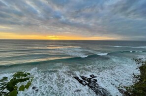 Paisagem costeira com ondas, céu claro e linha do horizonte.