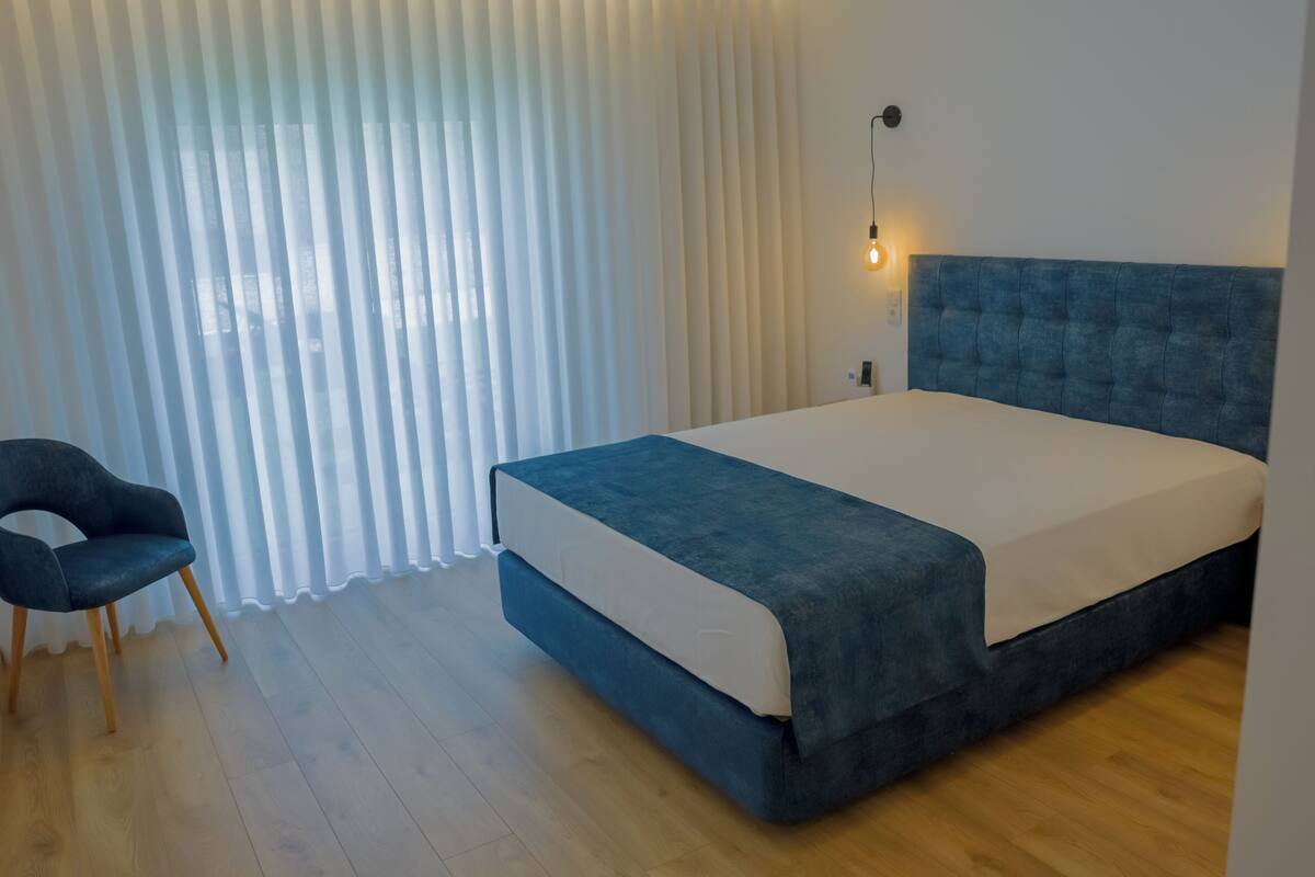 Quarto com cama, uma cadeira e janela com persianas.
