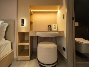 Quarto de hotel pequeno com uma cama, uma mesa com cadeira, um cesto de lixo e um vaso sanitário.