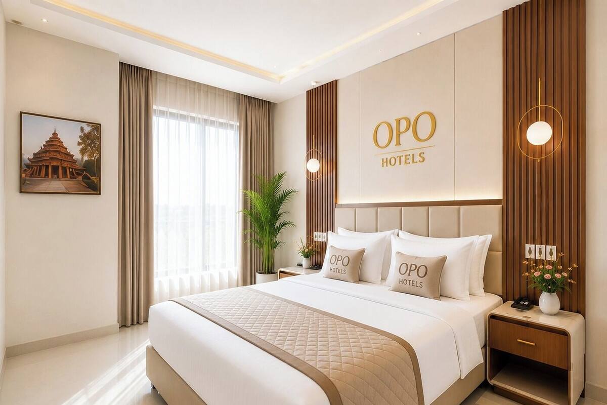 Quarto de hotel com uma cama grande, mesa de cabeceira com abajur, placa na parede e janela com cortinas.