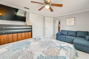 Sala de estar com ventilador de teto, televisão de tela plana, sofá azul e tapete estampado.