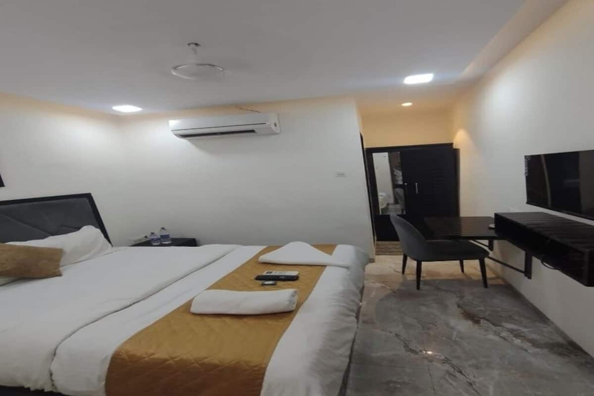 Quarto de hotel com cama, mesa de cabeceira, ar condicionado, escrivaninha, cadeira e televisão na parede.