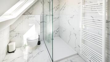 Uma casa de banho moderna com cabine de duche em vidro, sanita e radiador branco.