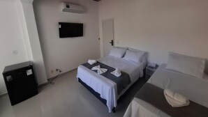 Quarto com cama, televisão de tela plana na parede, ventilador de teto e um pequeno armário preto.