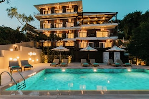 Um hotel com vários andares, piscina, área de estar ao ar livre e fachada bem iluminada.