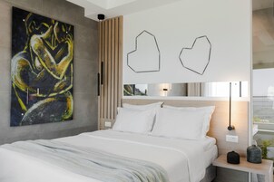 Quarto moderno com uma grande pintura abstrata, uma cama com roupa de cama branca, cabeceira de madeira e mesa de cabeceira com abajur.