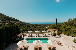 Área de piscina no terraço, com espreguiçadeiras, guarda-sóis e vista para o mar.