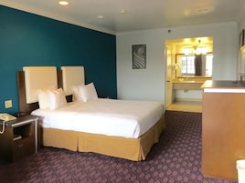 Quarto de hotel com cama, mesas de cabeceira, escrivaninha, espelho e banheiro visível por uma porta aberta.