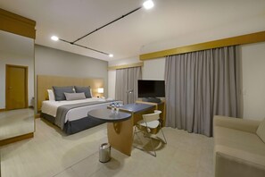 Quarto de hotel com uma cama, uma escrivaninha, uma cadeira, uma televisão e um sofá.