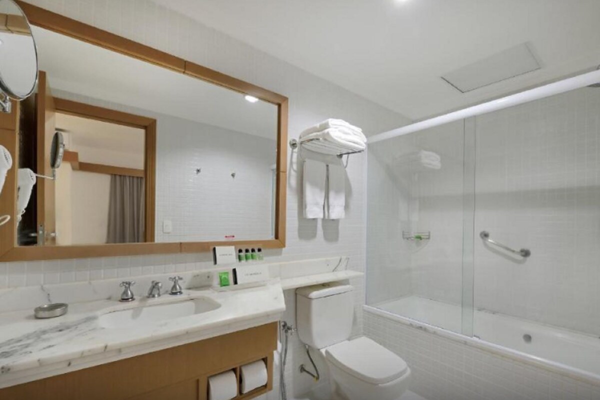 Uma casa de banho moderna com um espelho grande, lavatório, sanita e cabine de duche em vidro.