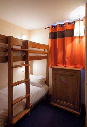 Uma cama de solteiro com cabeceira de madeira, um armário pequeno de madeira e uma cortina com padrão listrado.