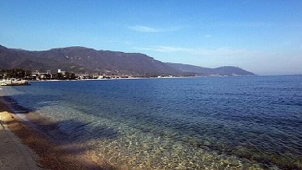 Vista costeira com águas cristalinas, uma praia e uma montanha ao fundo.