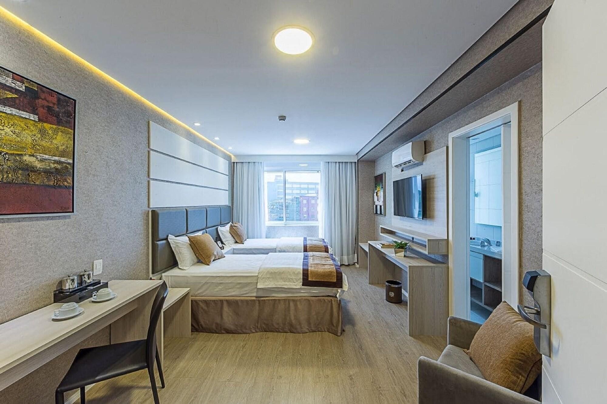 Quarto de hotel com cama, escrivaninha, cadeira, TV e vista para a cidade.