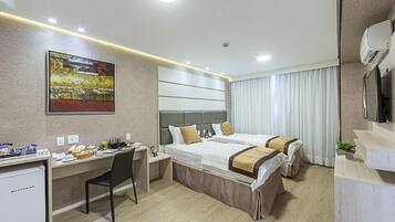 Quarto de hotel com duas camas, uma escrivaninha, uma cadeira, uma mesa de jantar e uma janela grande com cortinas.
