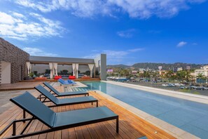 Uma piscina no terraço com espreguiçadeiras, área de estar coberta e vista para a paisagem urbana.