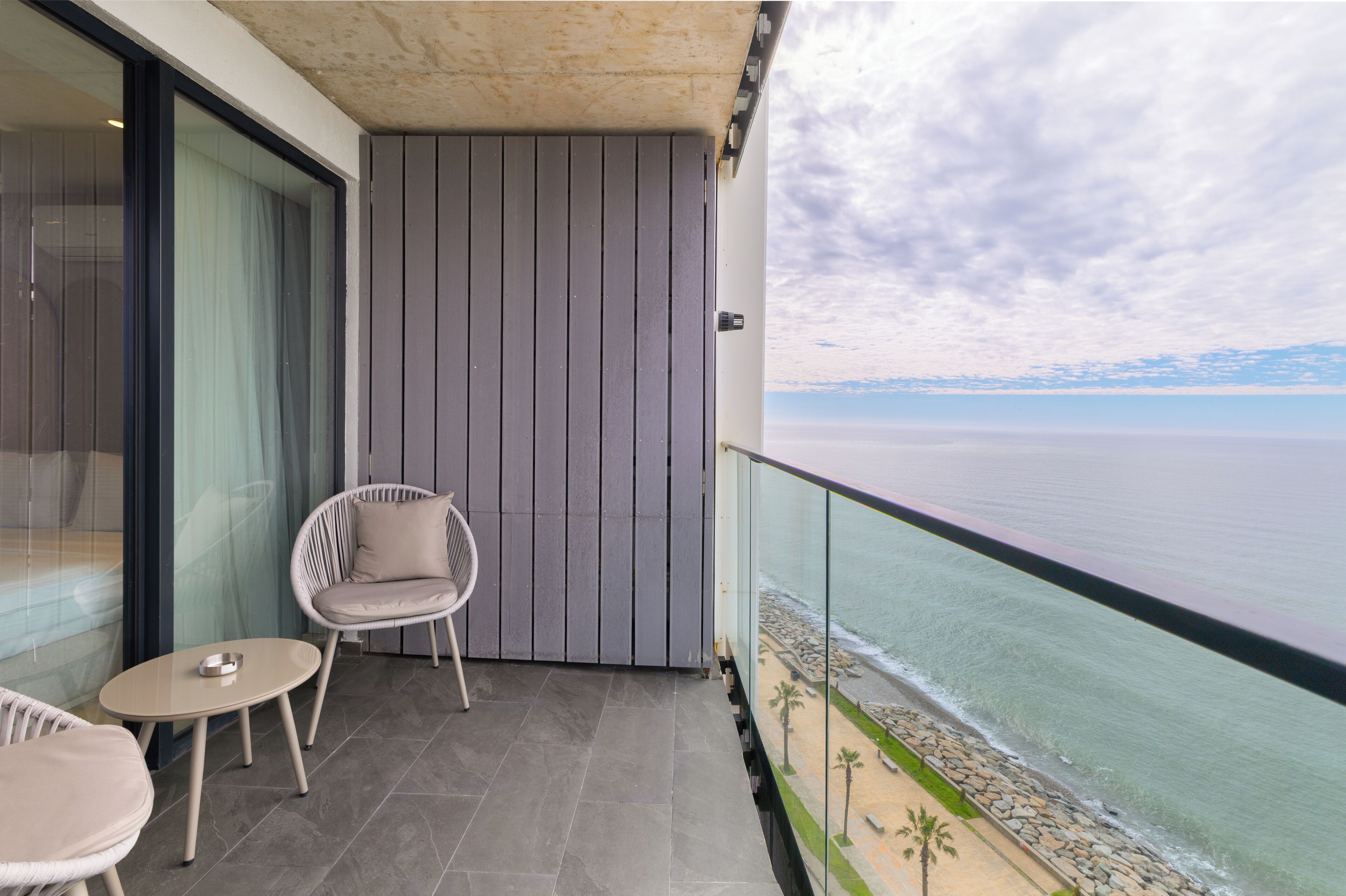 Varanda com vista para o mar, porta de vidro e duas cadeiras de vime.