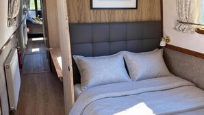 Corredor estreito que leva a uma cama com cabeceira e almofadas.