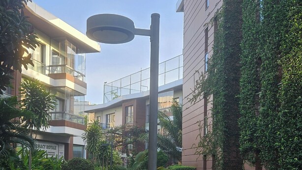Uma trilha leva a um edifício com placa de farmácia, cercado por vegetação e céu limpo.