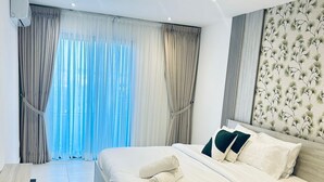 Quarto de hotel moderno com uma cama, cortinas, cabeceira estampada com flores e vista para o exterior.
