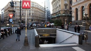 Uma rua urbana movimentada com entrada de estação de metro, edifícios históricos e uma estátua.