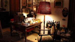 Uma área de refeições com uma mesa, cadeiras, uma luminária e diversos objetos sobre a mesa.