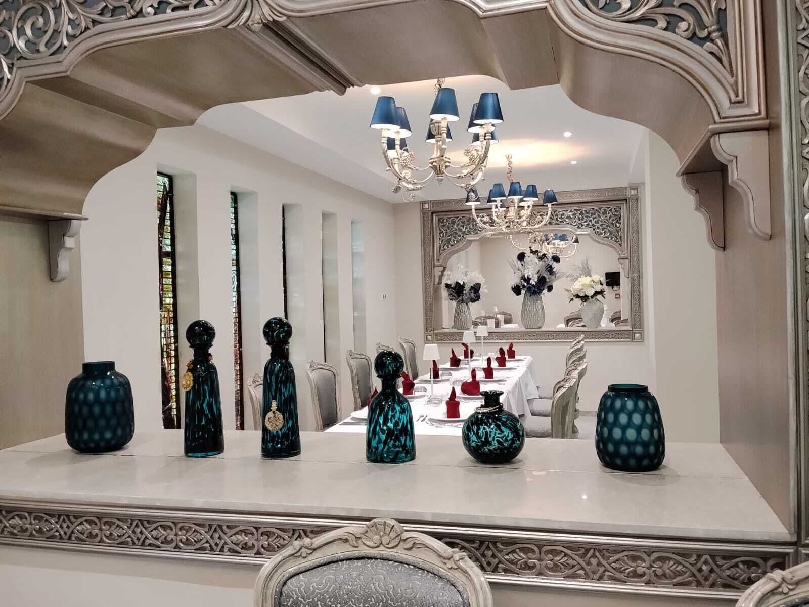 Uma sala de jantar com uma mesa branca posta para uma refeição, rodeada por decorações elaboradas e um espelho grande.