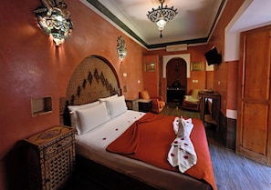 Quarto de hotel com uma cama, um painel decorativo, uma televisão e uma porta de madeira.