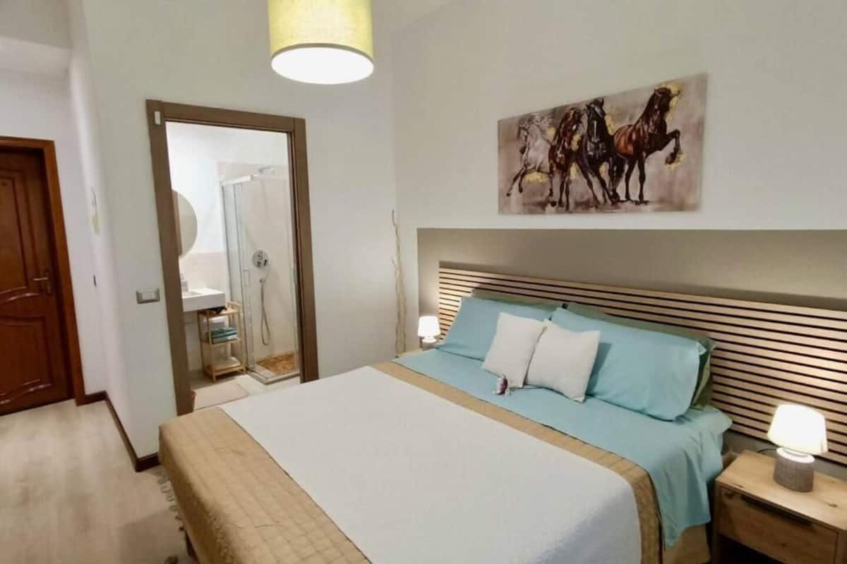 Quarto com cama, mesas de cabeceira, espelho, porta e uma obra de arte na parede.