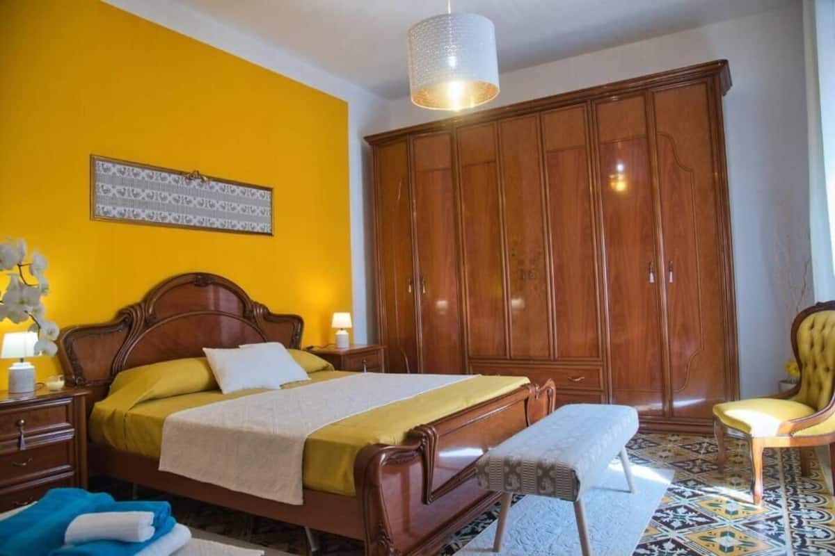 Quarto com cama de madeira, guarda-roupa espaçoso, um banco e soalho estampado.