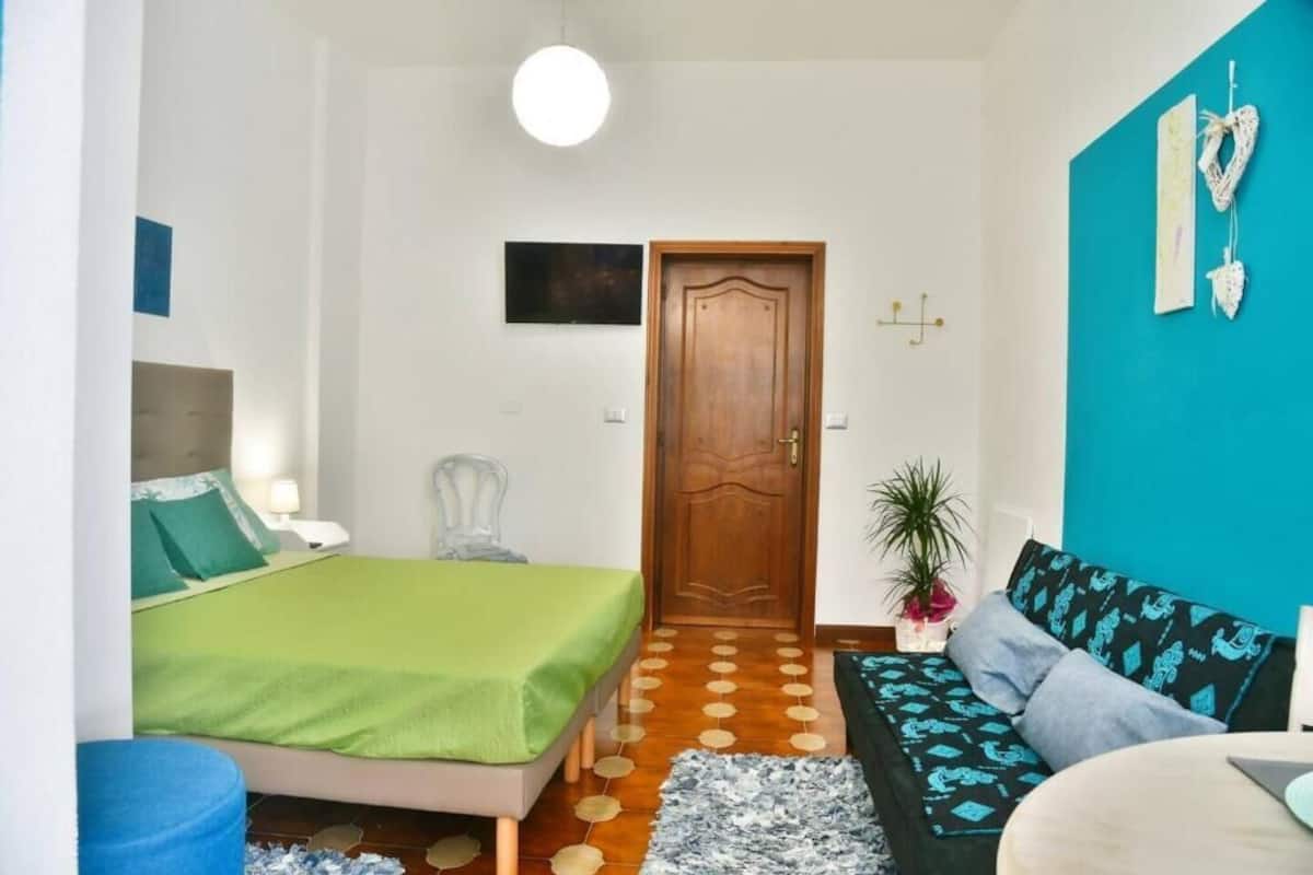 Quarto com cama, sofá, mesinha, planta em vaso e uma porta.