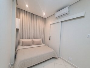 Quarto com cama, cortinas, ar condicionado e guarda-roupa.