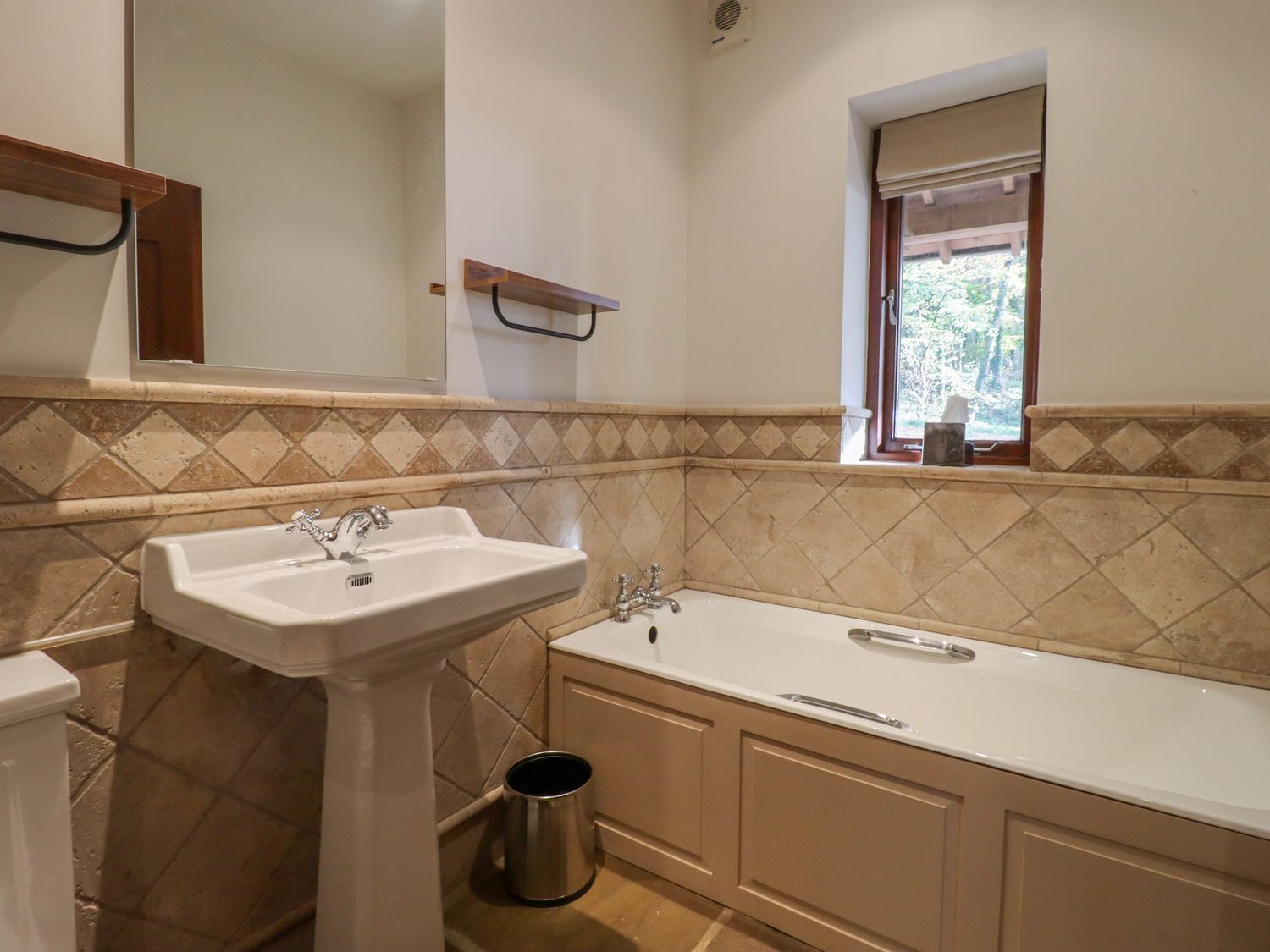 Casa de banho com lavatório assentado, toucador com espelho e janela com vista para vegetação.