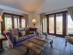 Um quarto aconchegante com um sofá roxo, uma mesa de centro de madeira e amplas janelas com cortinas.