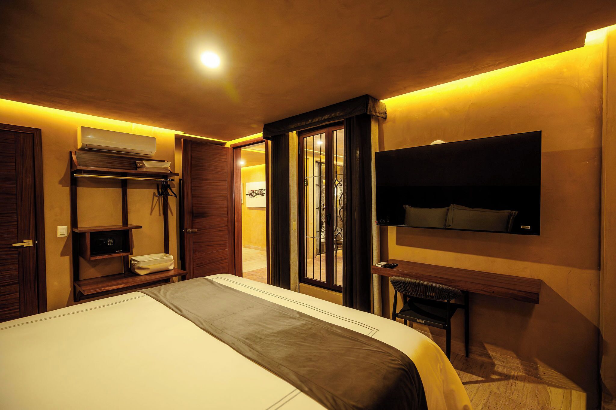 Quarto de hotel com uma cama, escrivaninha, televisão, guarda-roupa e ar condicionado.