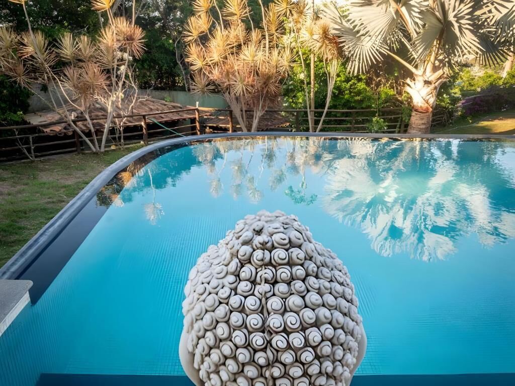 Uma piscina com um objeto decorativo no centro, cercada por palmeiras e um deck de madeira.