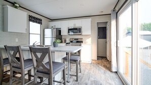 Uma cozinha moderna com armários brancos, micro-ondas, frigorífico e zona de refeições com cadeiras cinzentas.