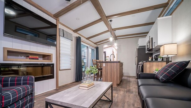 Cozinha moderna com vigas de madeira, área de refeições com mesa e cadeiras, e sala de estar com sofá e televisão.