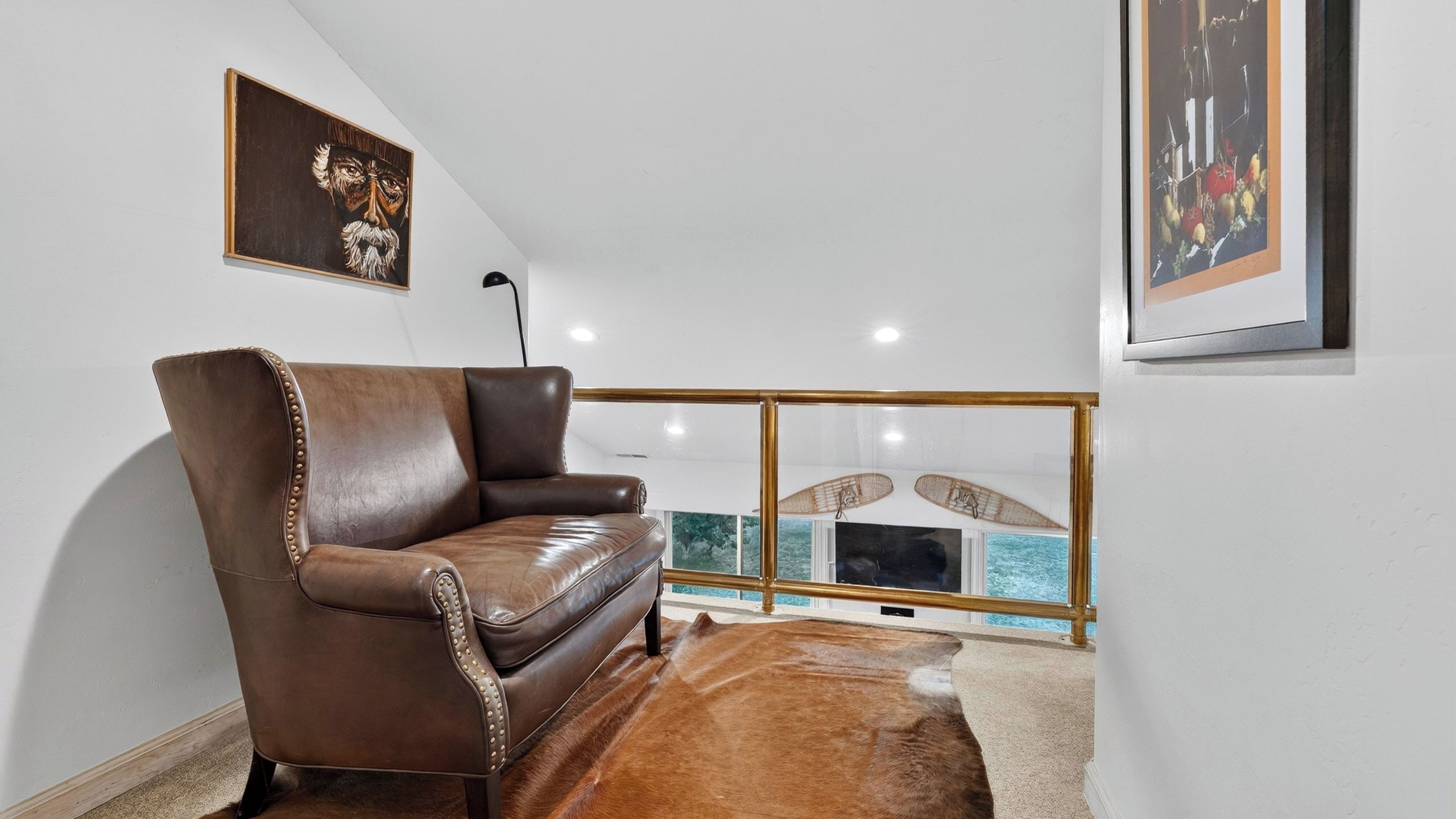 Quarto com sofá de couro, tapete de couro bovino e varanda com vista para áreas verdes.