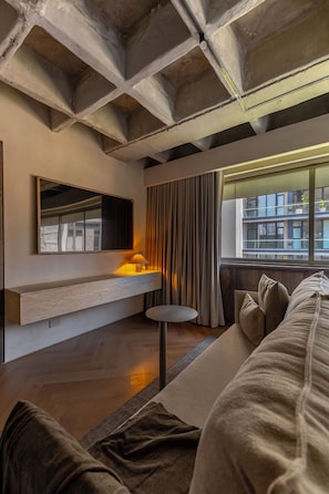 Uma sala de estar moderna com sofá, mesa lateral, abajur, janela grande com cortinas e espelho fixado na parede.