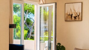 Quarto com porta de vidro deslizante para uma varanda, televisão de tela plana, sofá cinza e quadro com barcos à vela.