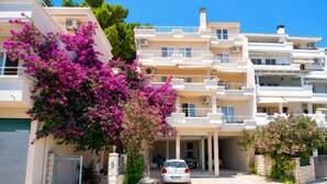 Um edifício residencial de vários andares com varandas, um carro estacionado em frente e flores de bougainvillea.