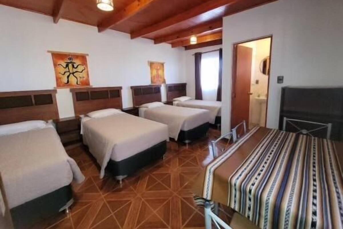 Quarto de hotel com três camas, teto de madeira e tapete estampado.