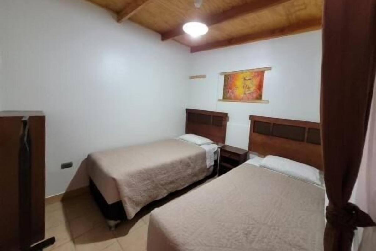 Quarto com duas camas, cabeceiras de madeira, ventilador de teto e uma luminária fixada na parede.