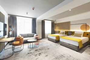 Quarto de hotel moderno com sofá, duas camas, uma mesinha e televisão.