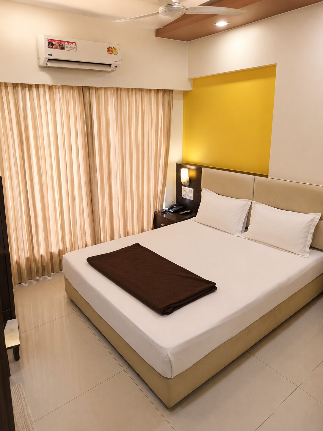 Quarto de hotel com cama, mesa de cabeceira, aparelho de ar condicionado e cortina.