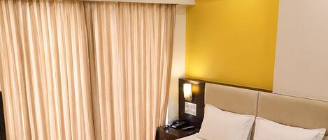 Quarto de hotel com cama, mesa de cabeceira, aparelho de ar condicionado e cortina.