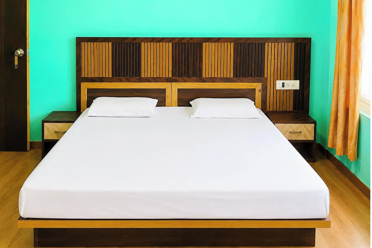 Uma cama de casal com cabeceira de madeira, duas mesas de cabeceira e uma parede verde.