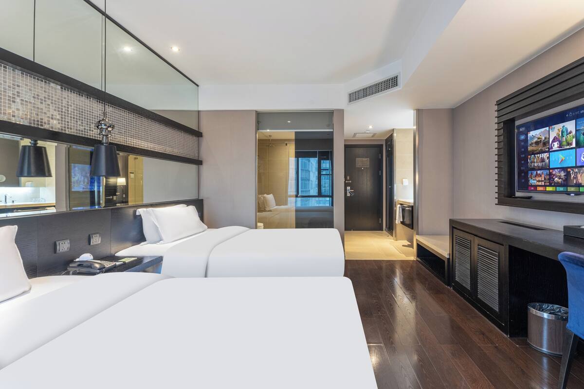 Quarto de hotel com duas camas, televisão, escrivaninha e uma janela grande.
