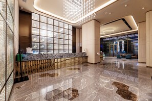 Um lobby moderno com piso de mármore, balcão de recepção e um amplo painel de vidro com padrão decorativo.